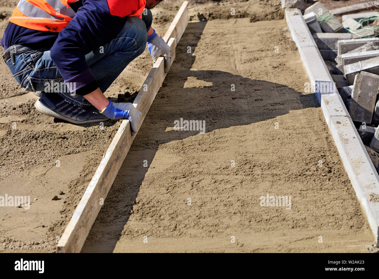 On the sidewalk, a worker cleans and levels the sandy platform with a ...