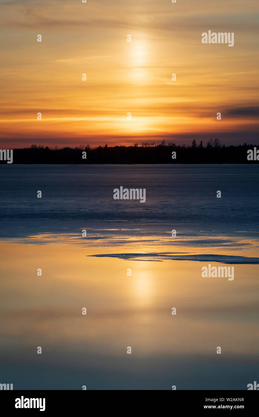 Light pillar in sunset reflecting from melting lake water Stock Photo ...
