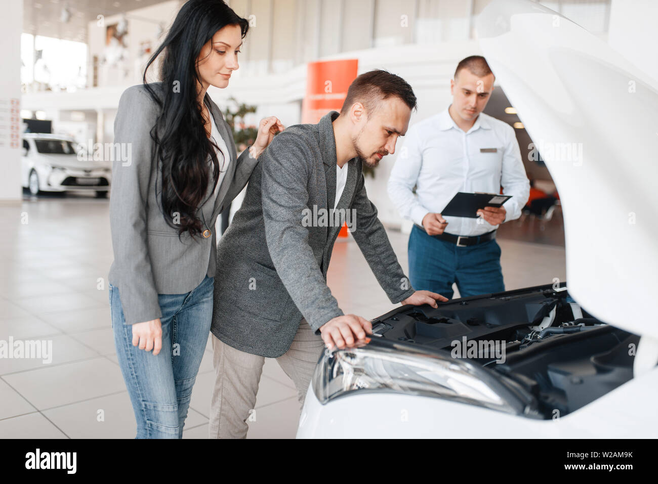 Manager shows the couple a new car in showroom. Male and female ...