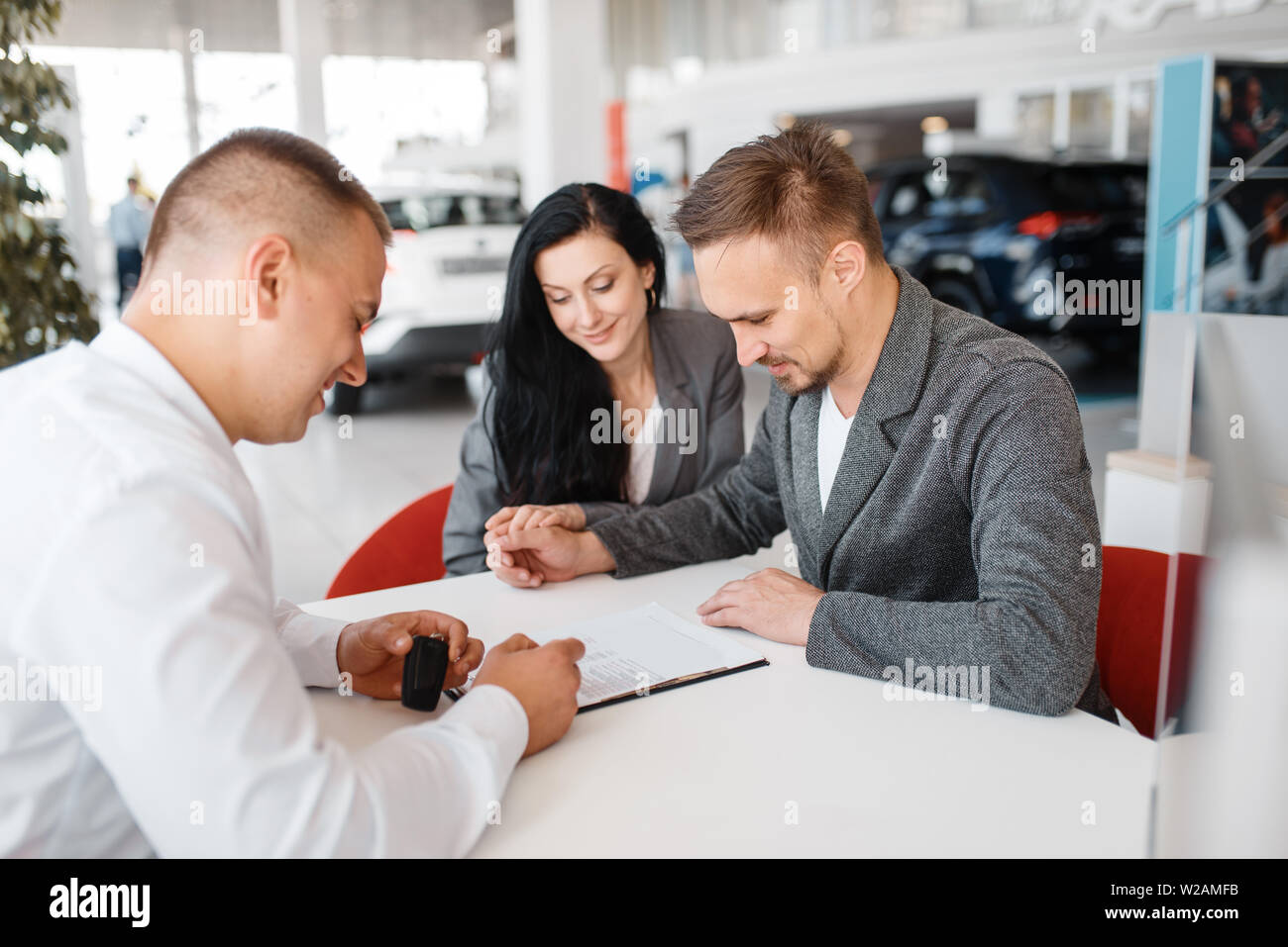 Salesman and a couple make out the sale of a new car in the showroom ...