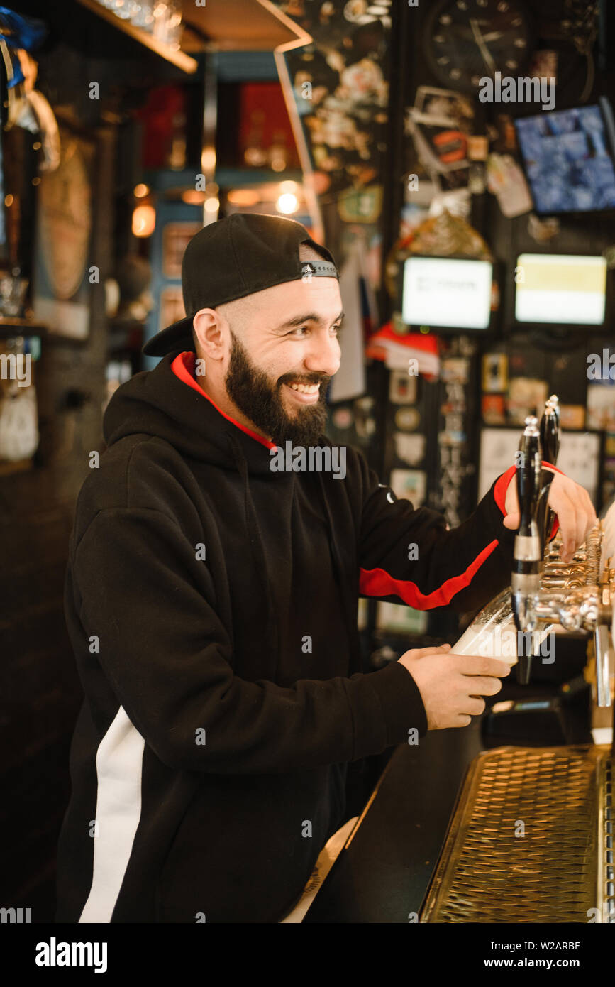 smiling barman pouring beer in a bar. Bearded courageous man pours you ...