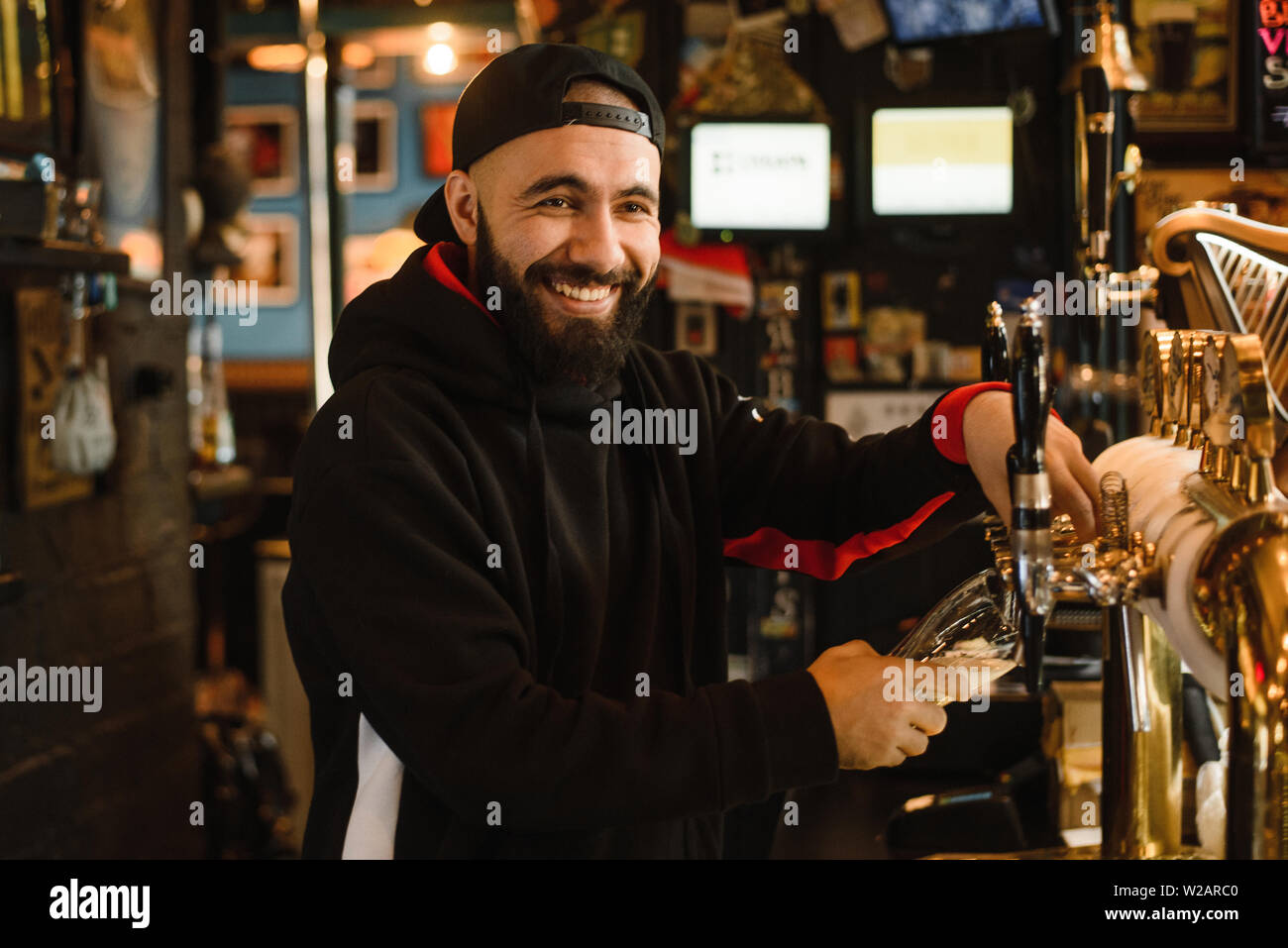 smiling barman pouring beer in a bar. Bearded courageous man pours you ...