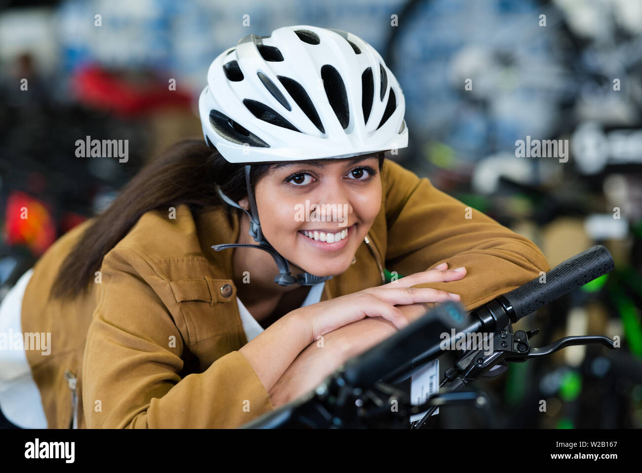portrait of young woman leaning over bicycle handlebars wearing helmet ...