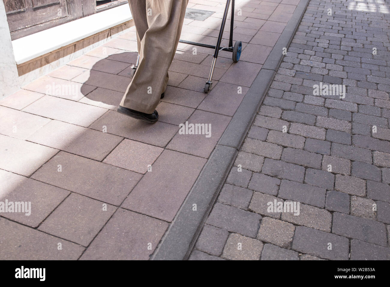 Elderly man walks by lowered sidewalk with walker. Urban accessibility ...