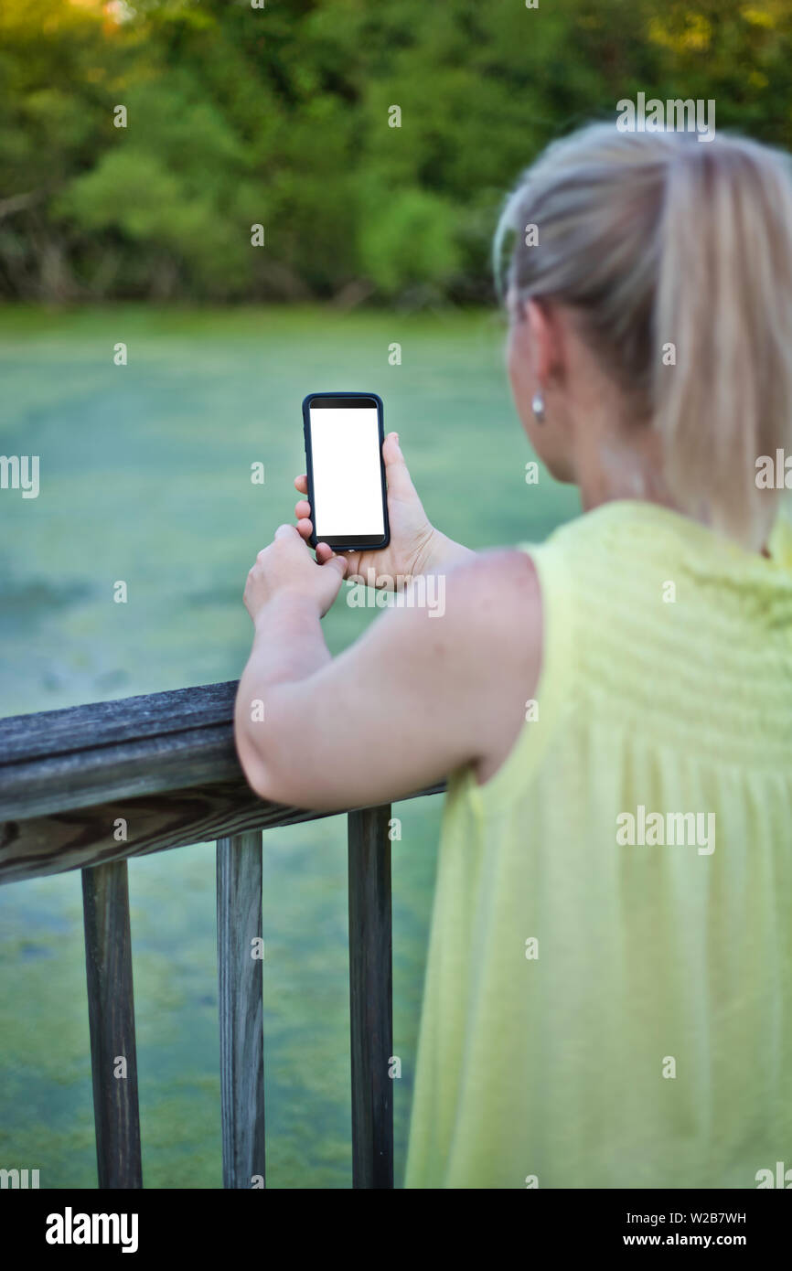 blonde woman looking at cell phone in front of scummy pond - screen ...