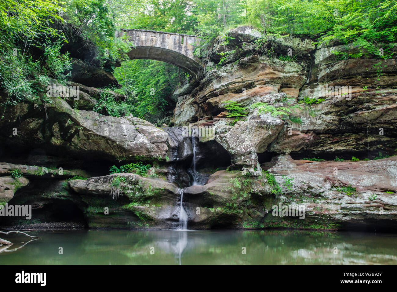 Ancient stone footbridge crosses over a ravine with a waterfall flowing ...