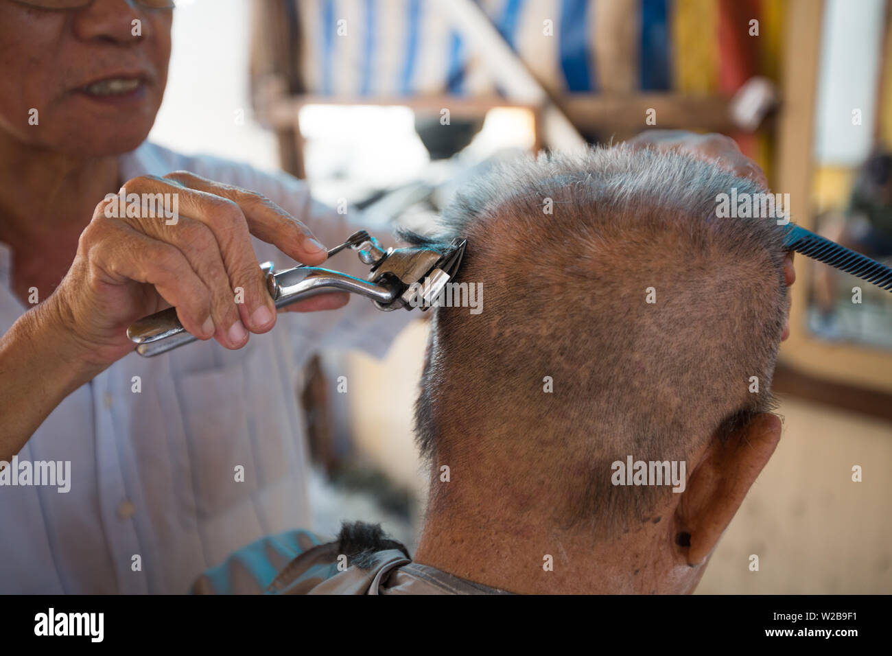 A street barber using hair hand clipper to cut his customer hair ...