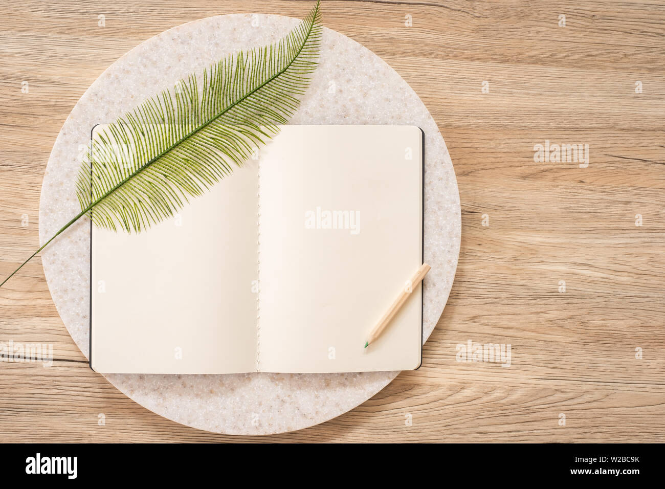 top view of open notebook with leaf and pencil on wooden table with ...