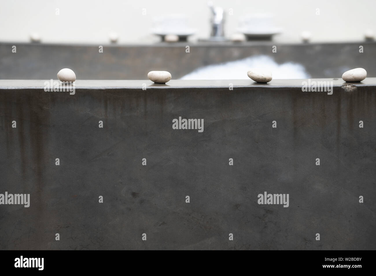 Stone bath filled with hot water and foam. At the edges of the bath are ...