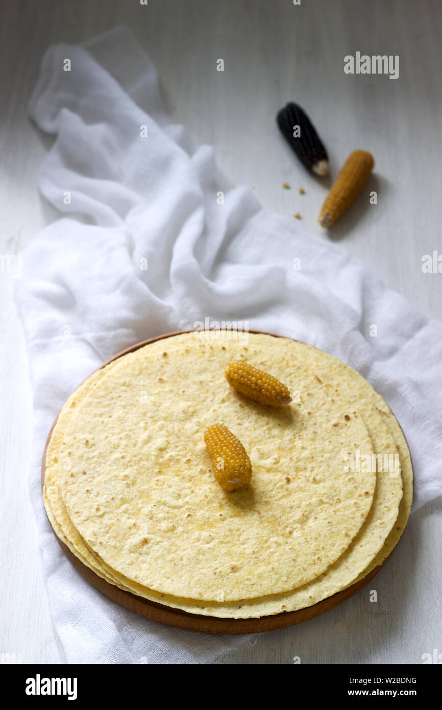 A stack of round corn tortillas on a wooden board and corncobs ...