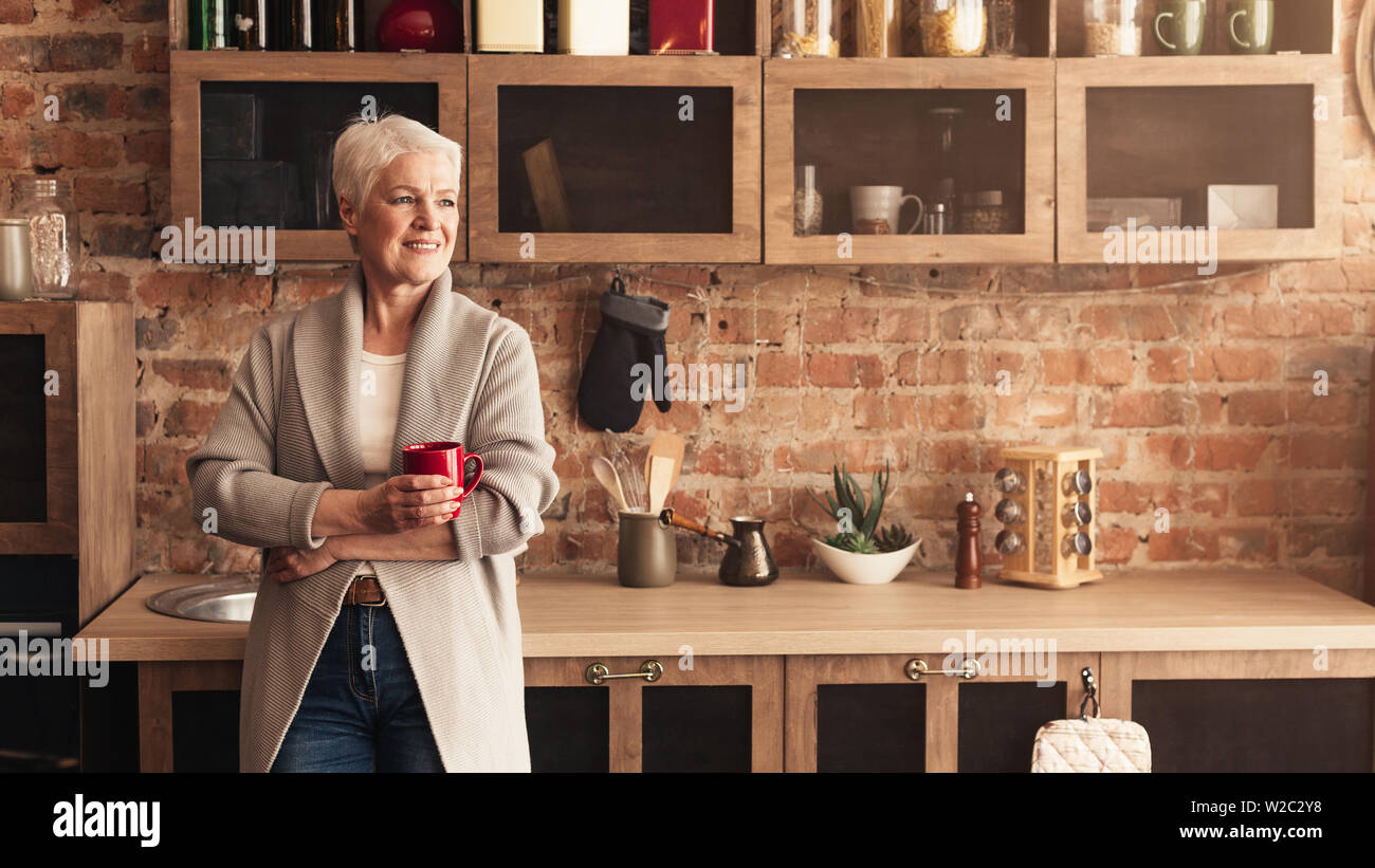 Calm senior lady standing at kitchen, drinking coffee Stock Photo - Alamy