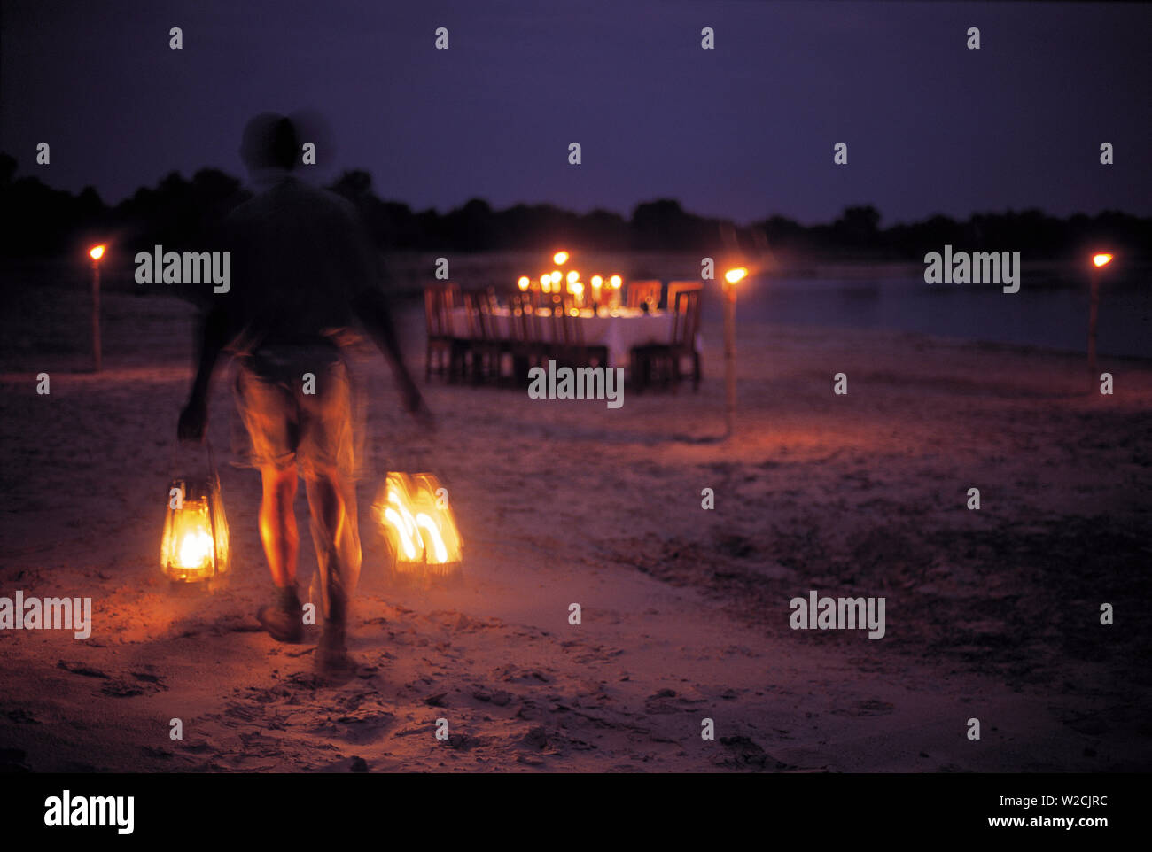 Staff at Safari lodge prepare bush dinner on a sand river bank under ...