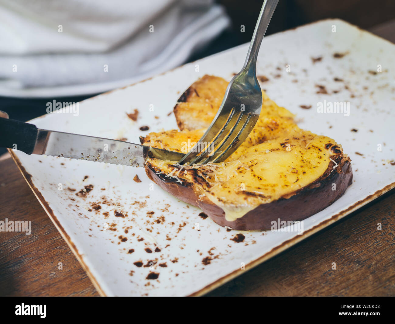 Close-up hands using knife and fork to cut cheese toast in white ...