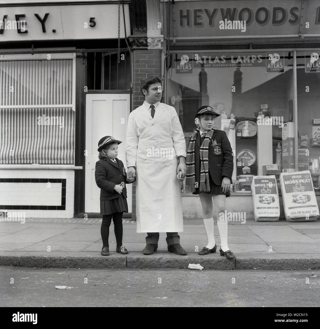 1970s, historical, a butcher helping two young school children to cross ...