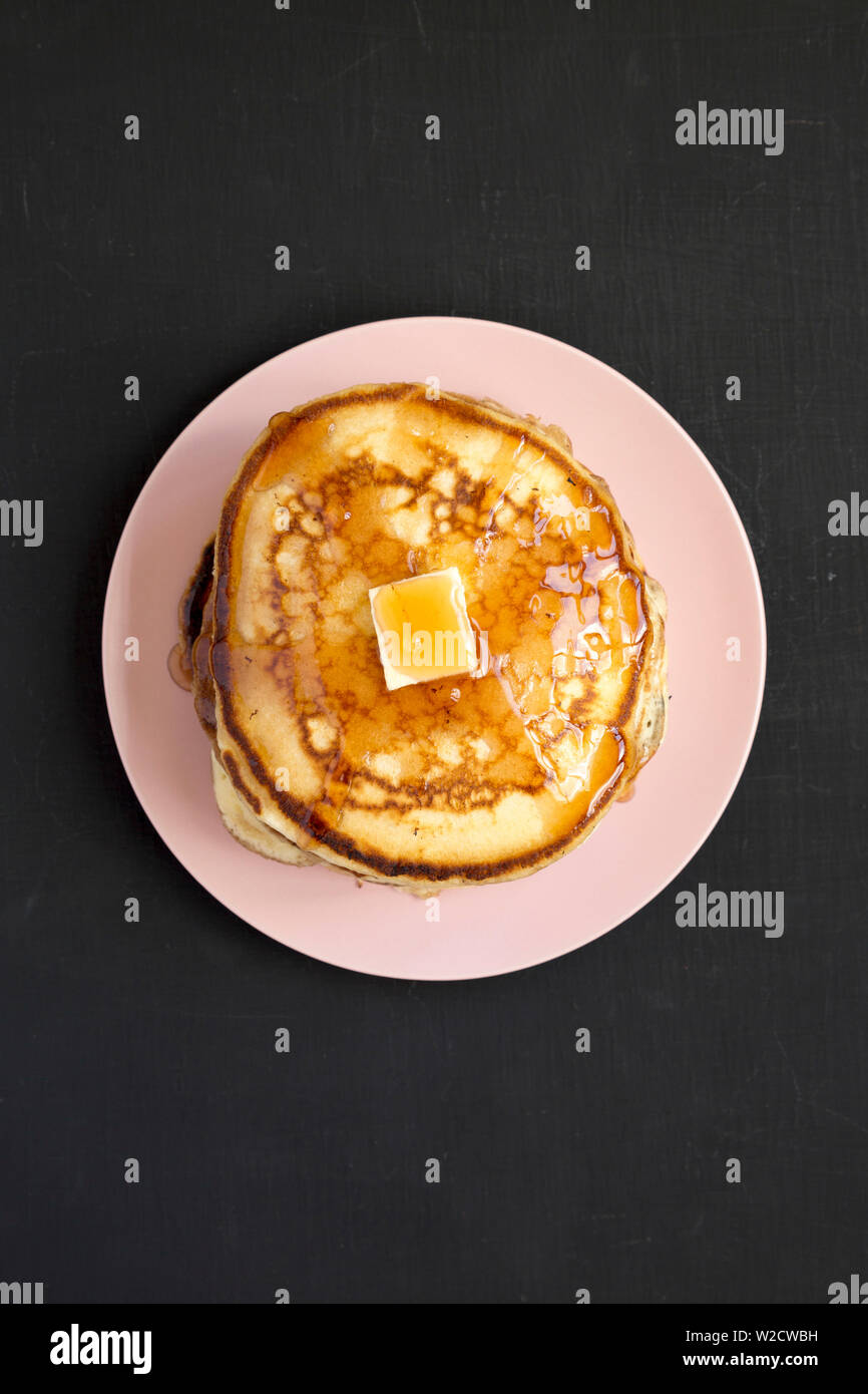 Homemade pancakes with butter and maple syrup on a pink plate, top view ...