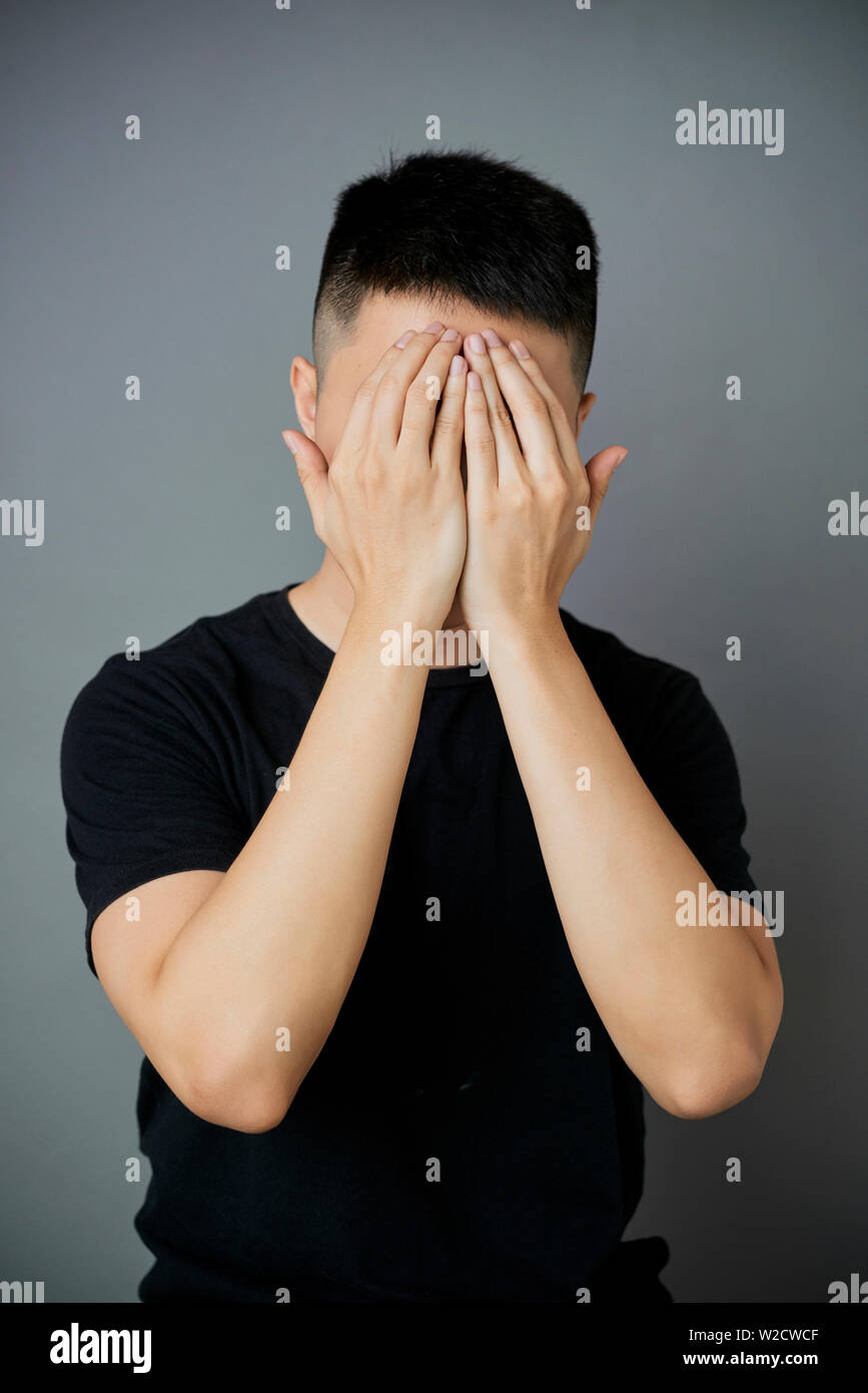 Portrait of young man standing in black T-shirt and hiding his face ...