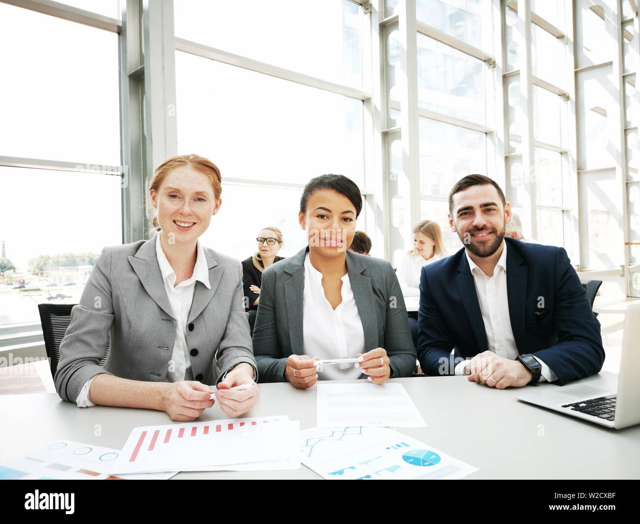 Three smiling business people at conference table with reports ...