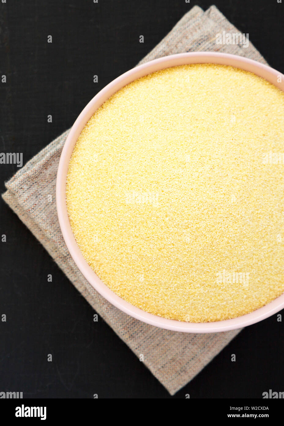 Dry semolina durum flour in a pink bowl over black background, overhead ...
