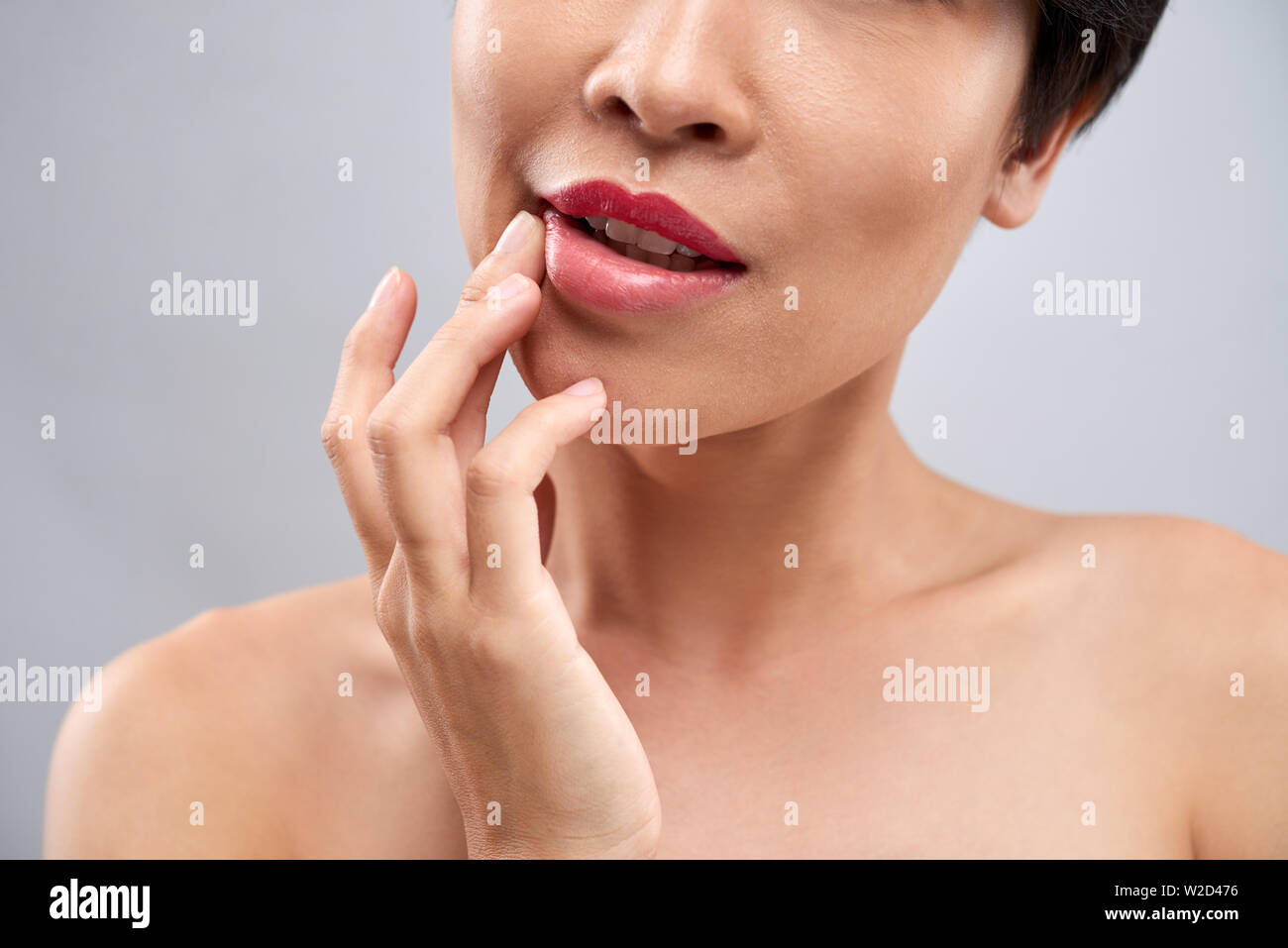 Close-up of young woman with lipstick on her lips touching her face ...