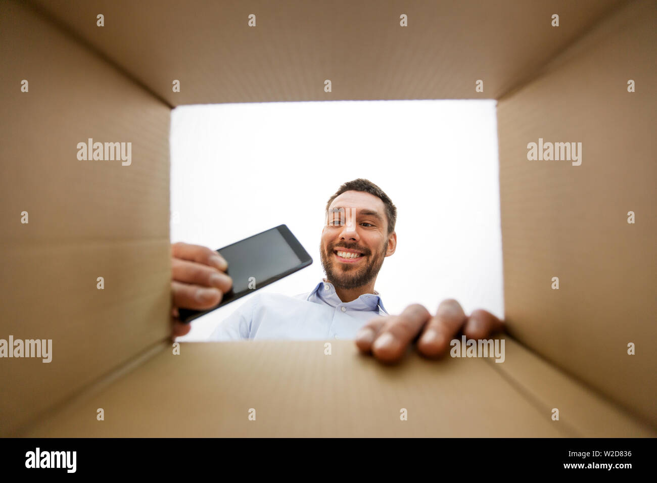 smiling man taking smartphone out parcel box Stock Photo - Alamy