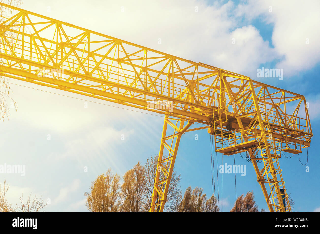 Yellow gantry crane behind the trees on the territory of the enterprise ...