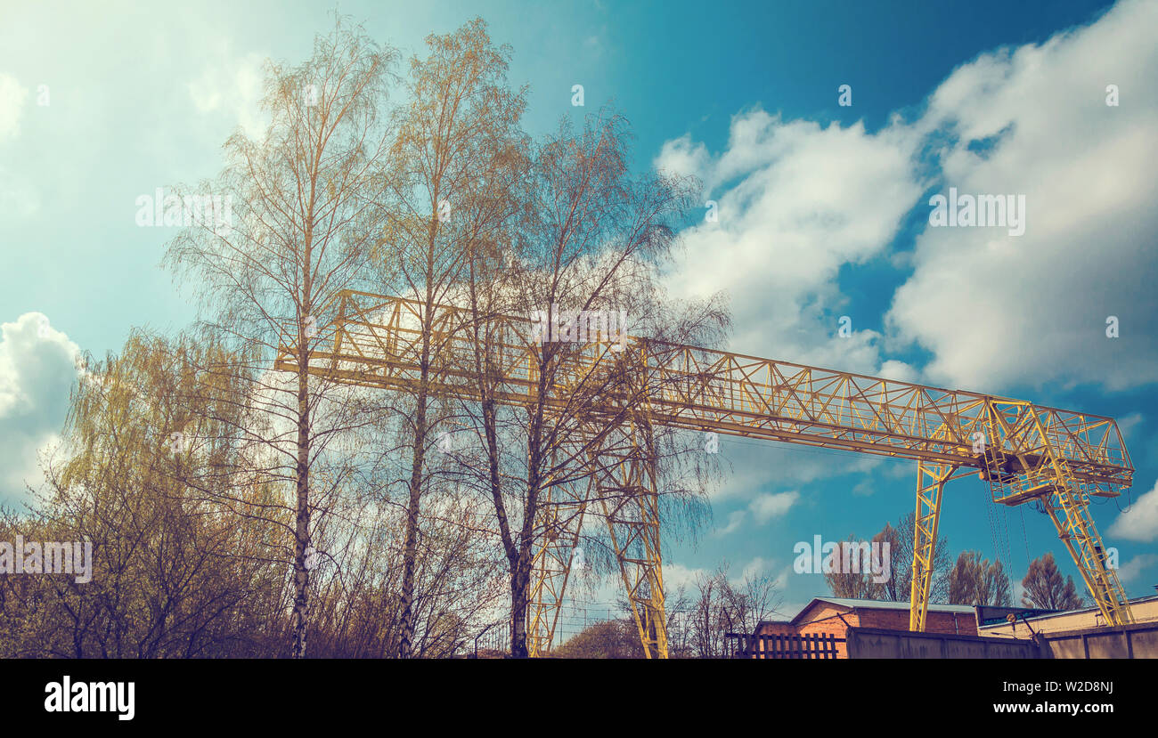 Yellow gantry crane behind the trees on the territory of the enterprise ...