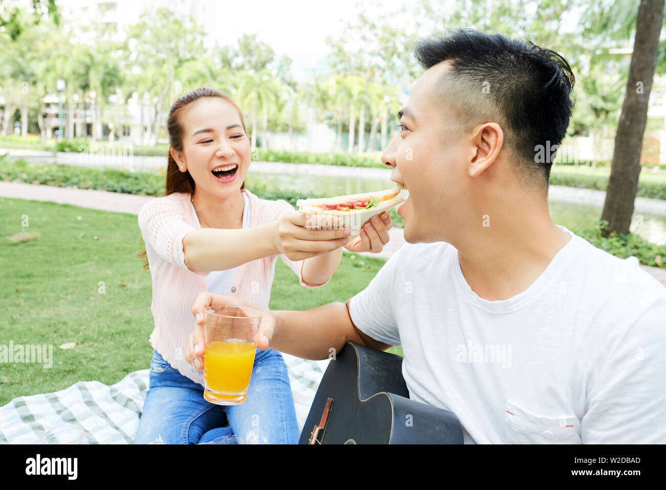 Happy Asian woman feeding her boyfriend with sandwich and juice while ...