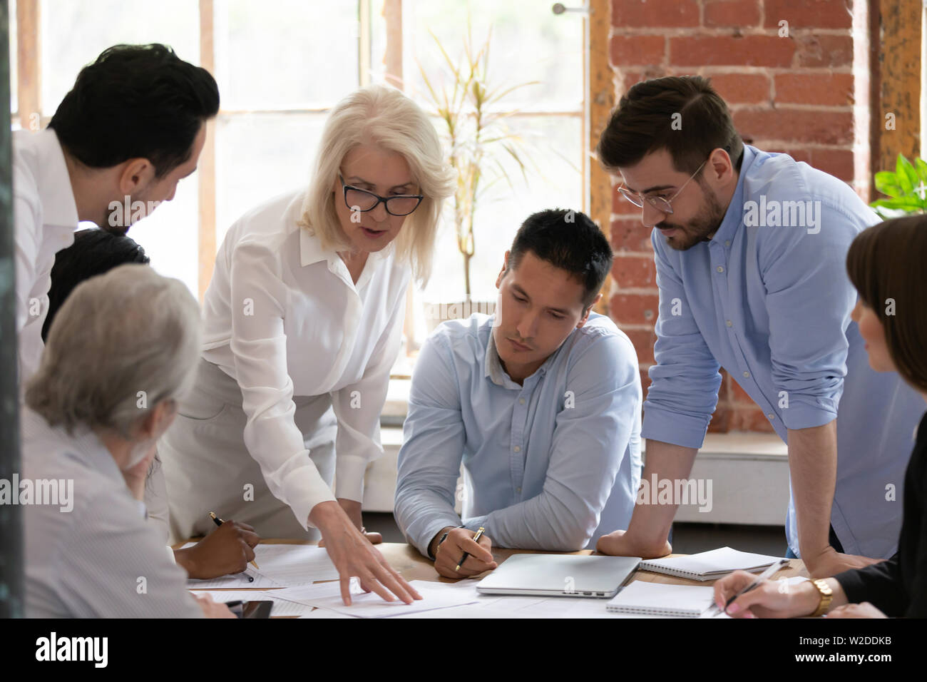 Serious old woman leader coach teach young workers explain paperwork ...