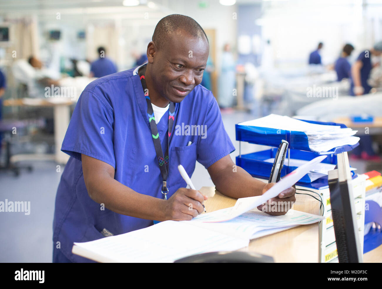Male NHS nurse at a workstation in a hospital ward dealing with patient ...