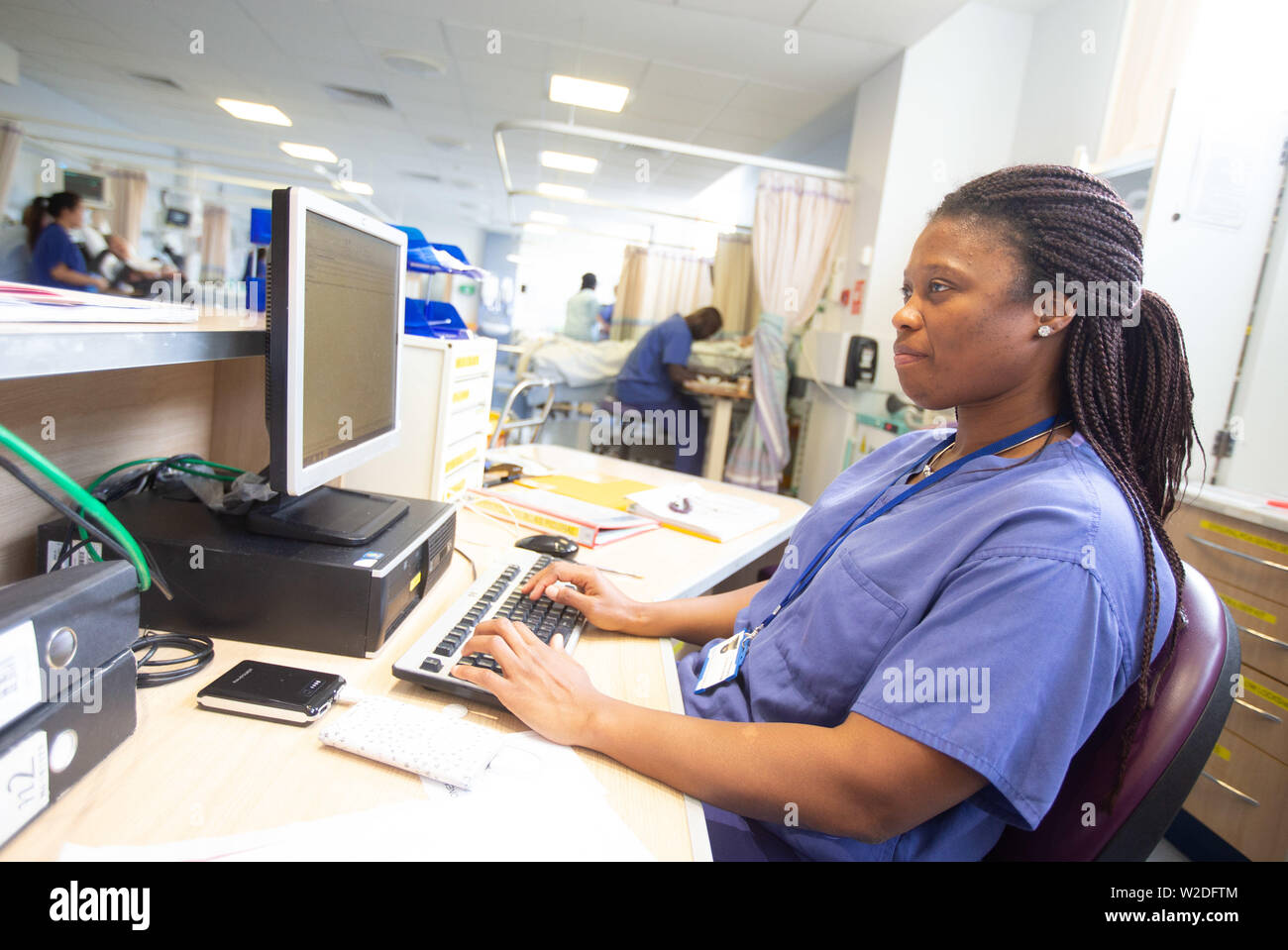 NHS nurse at a workstation in a Hospital ward dealing with inquiries ...