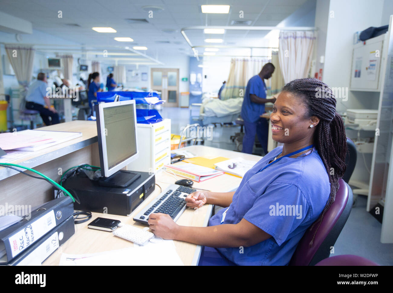 NHS nurse at a workstation in a Hospital ward dealing with inquiries ...