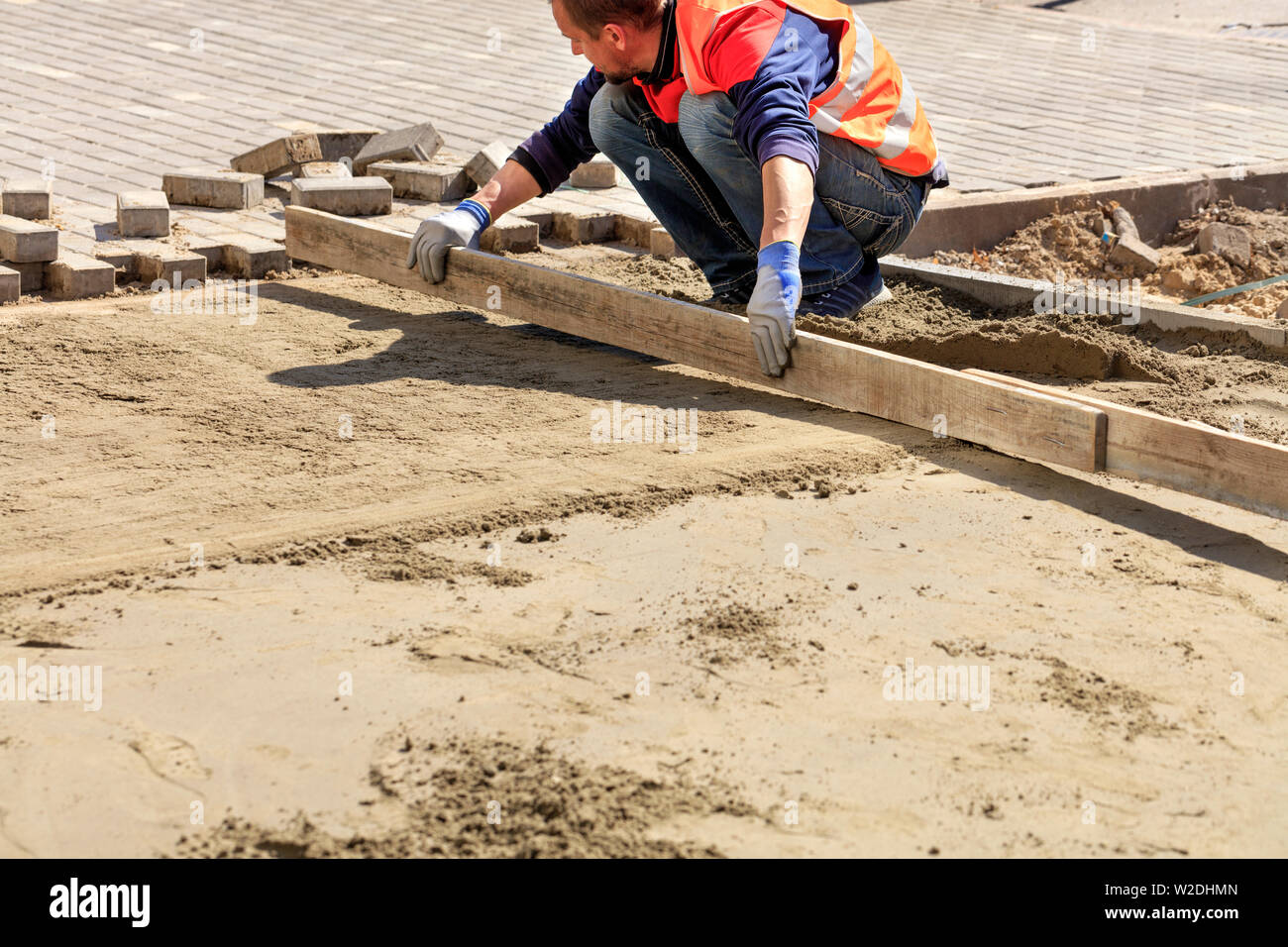 On the sidewalk, a worker aligns the sand platform with a wooden board ...
