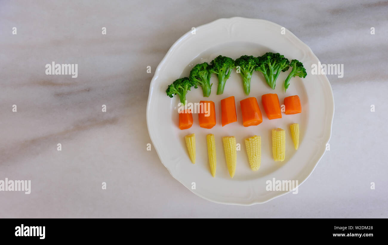 Arrangement of broccoli, baby corn and carrot, on a white plate placed ...