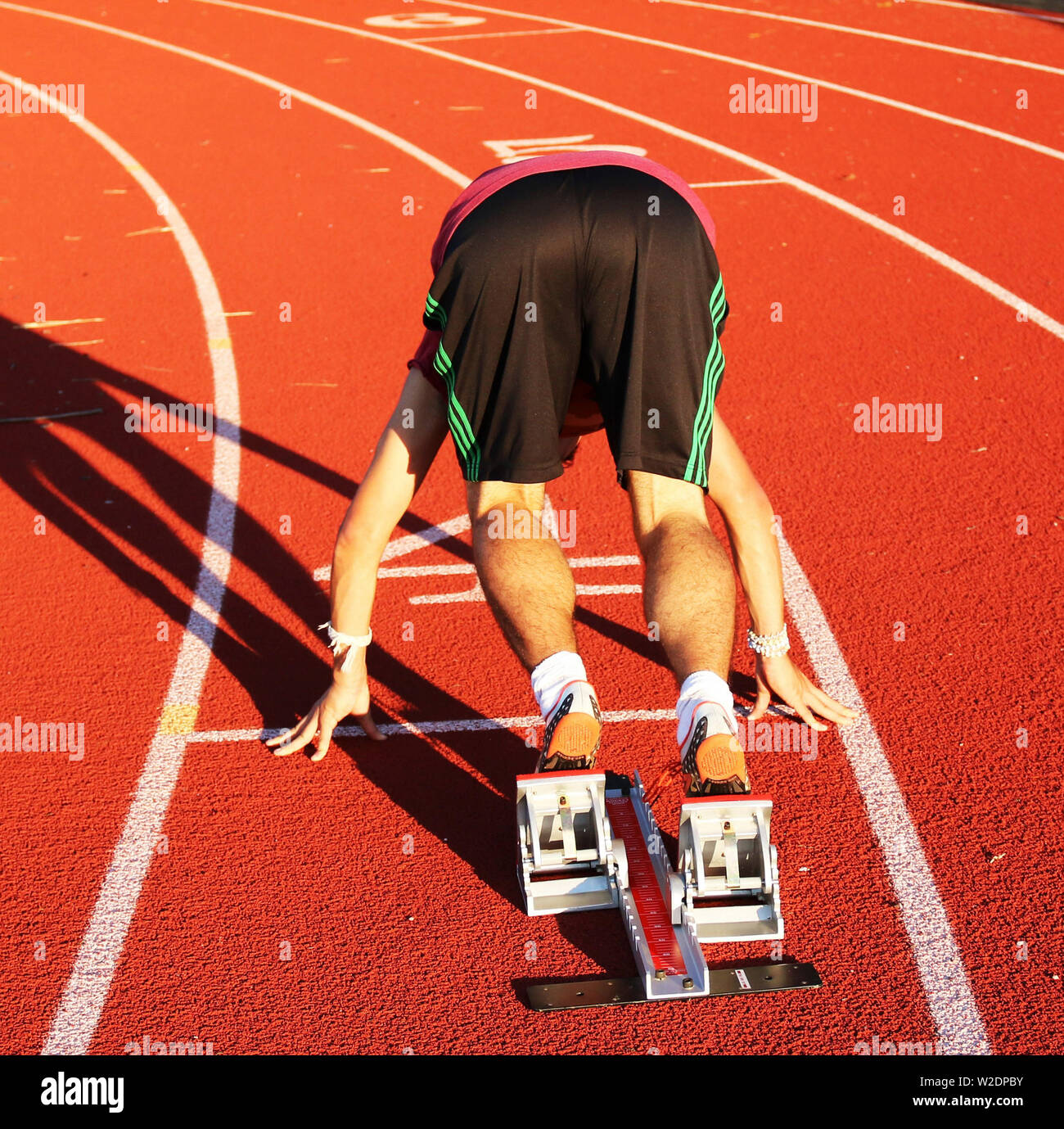 A high school track and field sprinter is in the set position in his ...