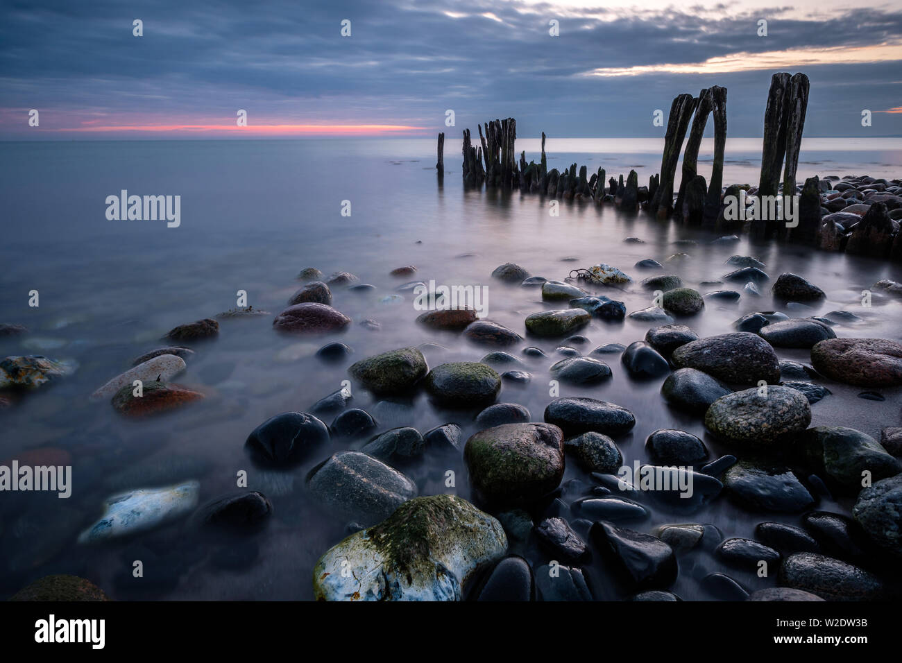 Cool and cloudy sunrise at stony beach of baltic sea with silhouette of ...