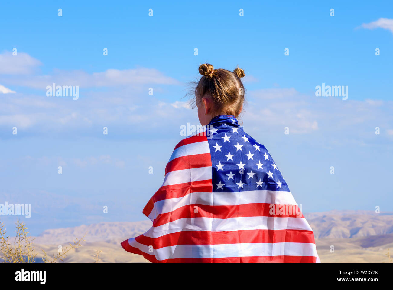American flag. Back view little patriotic happy girl wrapping in usa ...