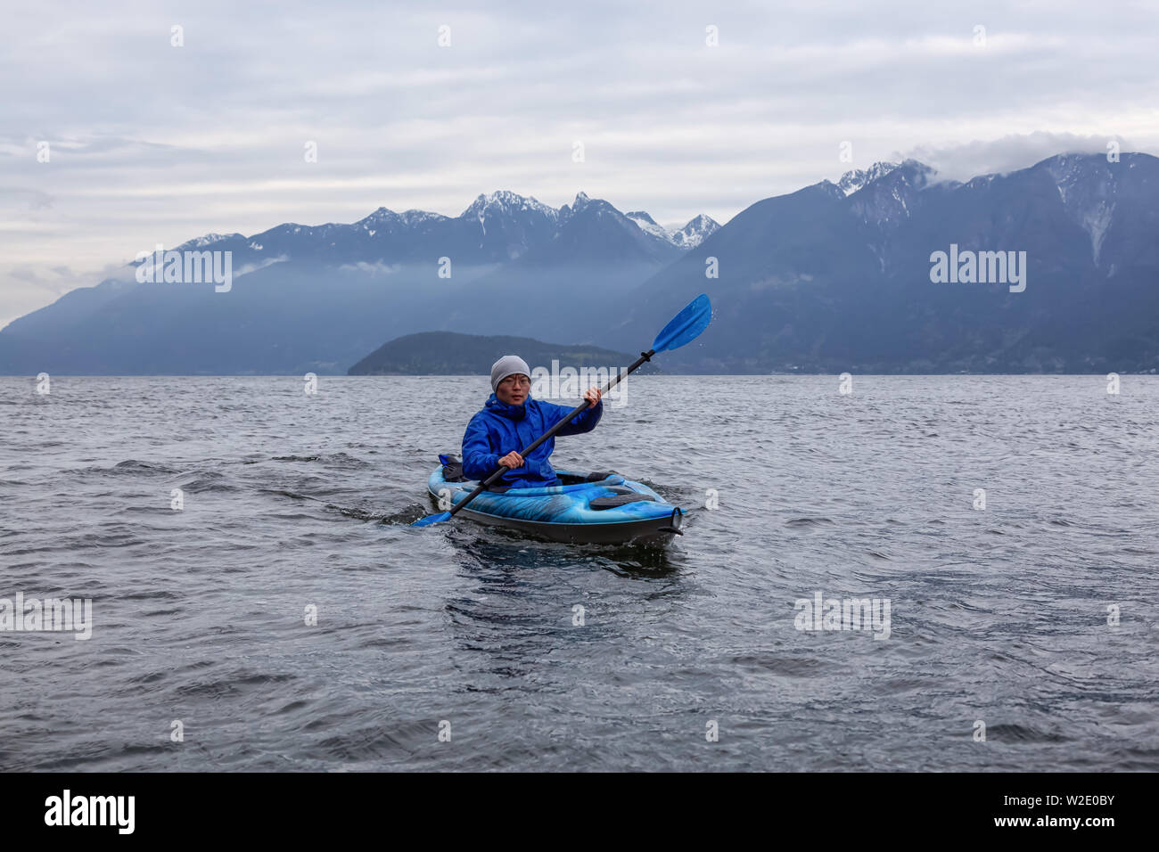 Adventurous man on a kayak is paddling in Howe Sound during a cloudy ...