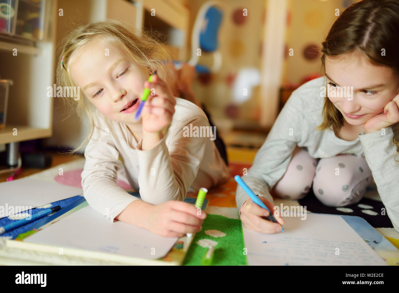 Two cute little sisters writing letters together at home. Older sister ...