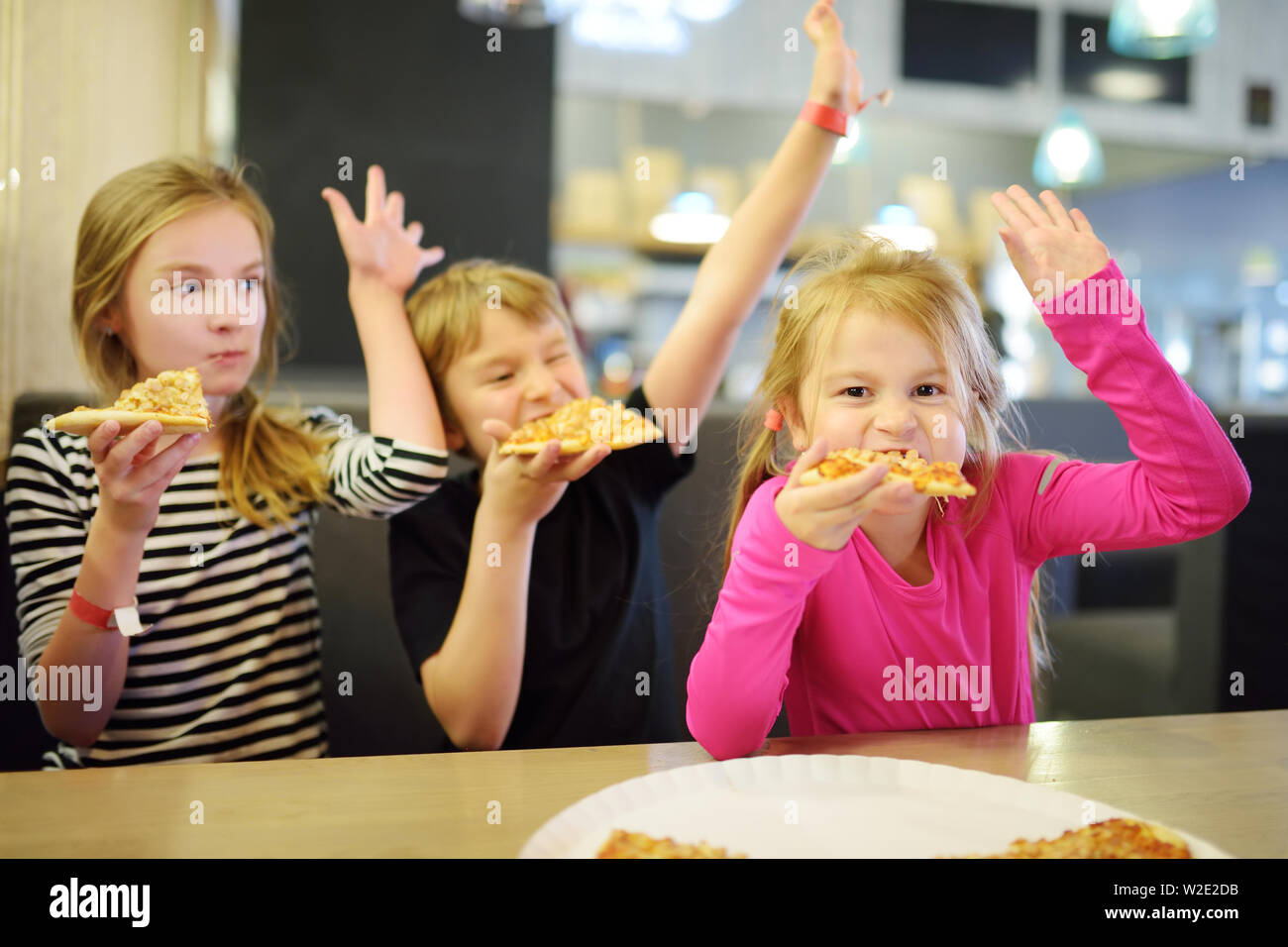 Three cute funny little siblings eating slices of pizza at indoor ...