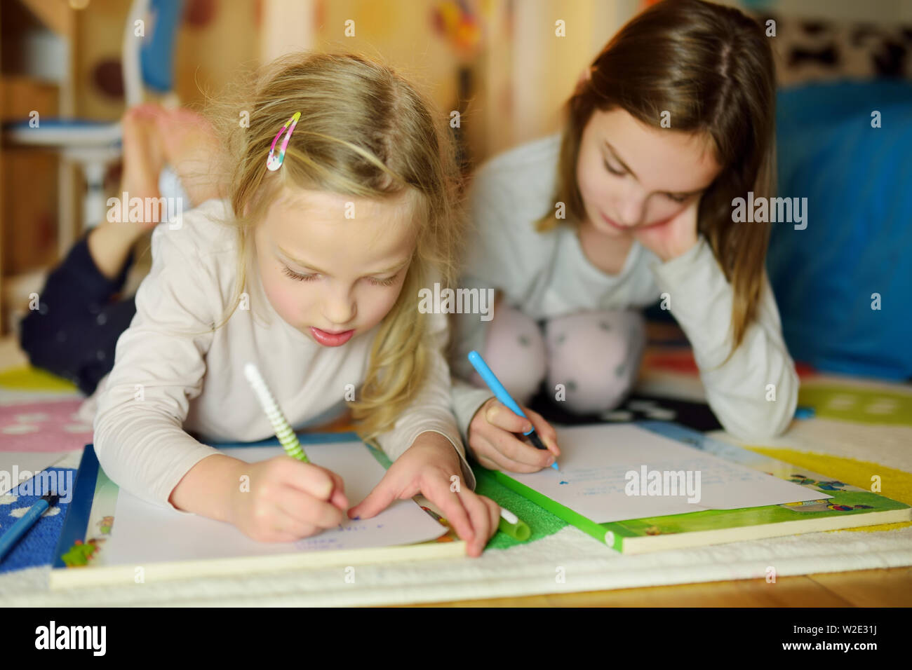 Two cute little sisters writing letters together at home. Older sister ...