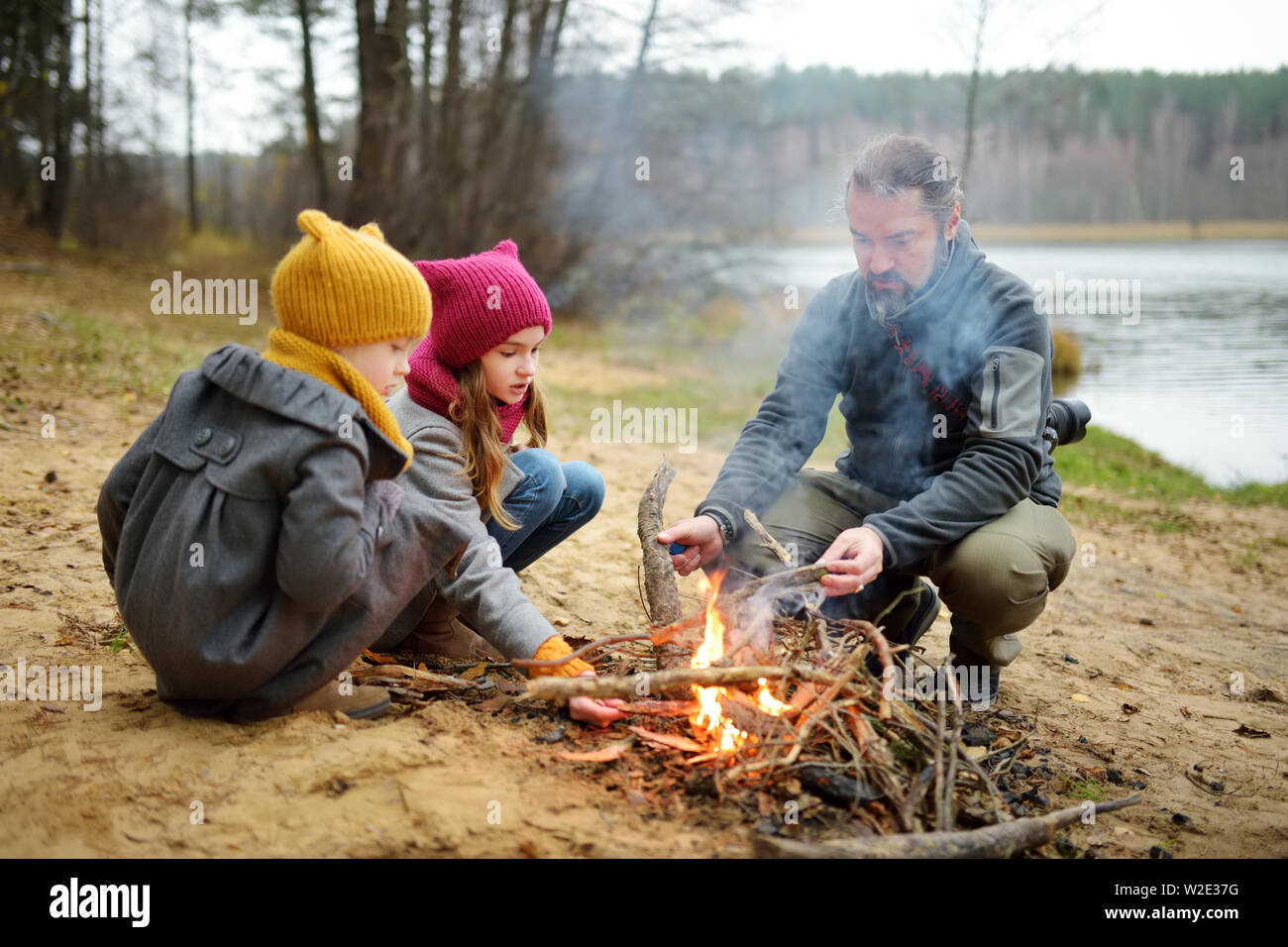 Cute little sisters and their father sitting by a bonfire on cold ...