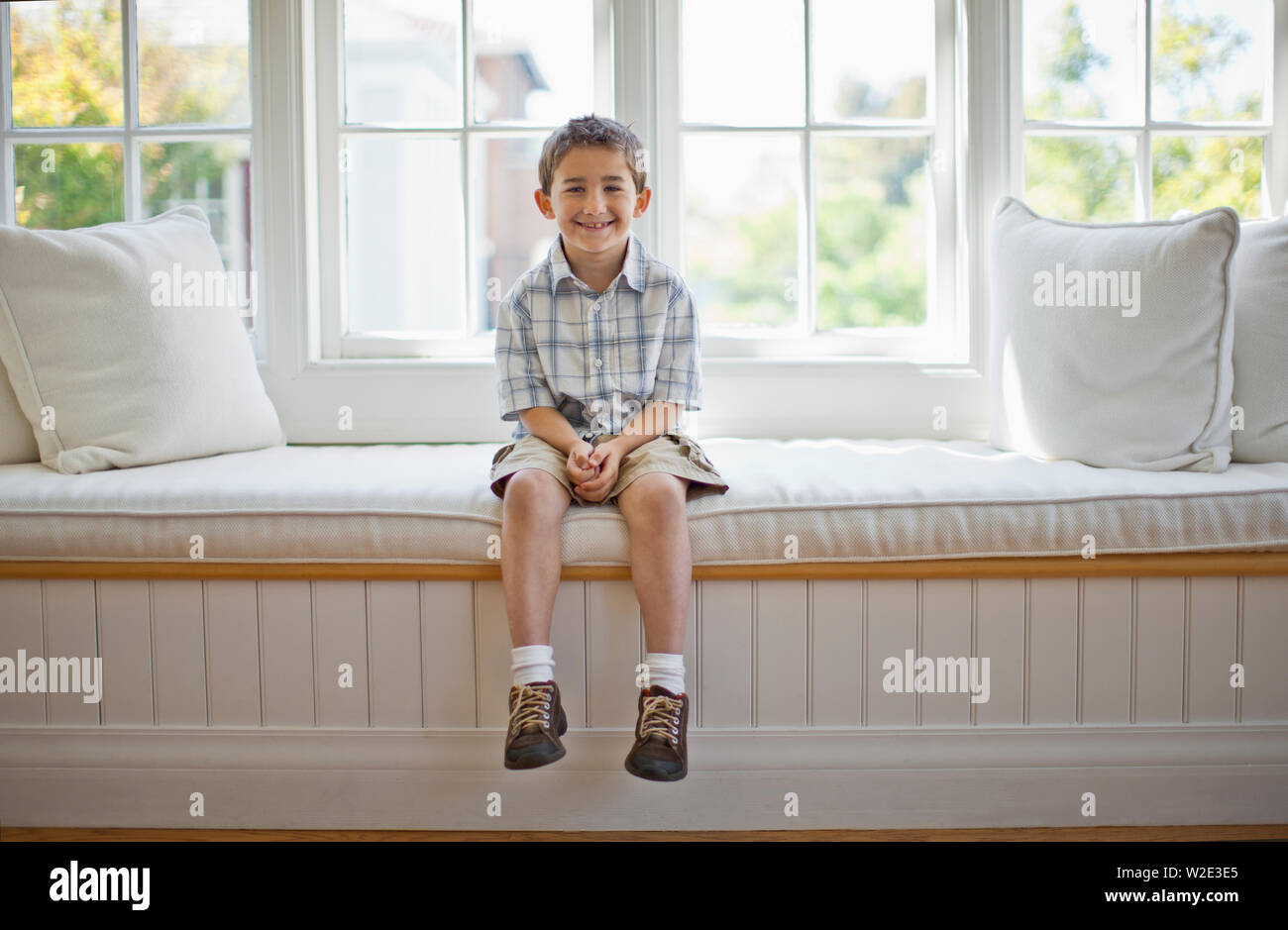 Portrait of a smiling young boy sitting on a window seat Stock Photo ...