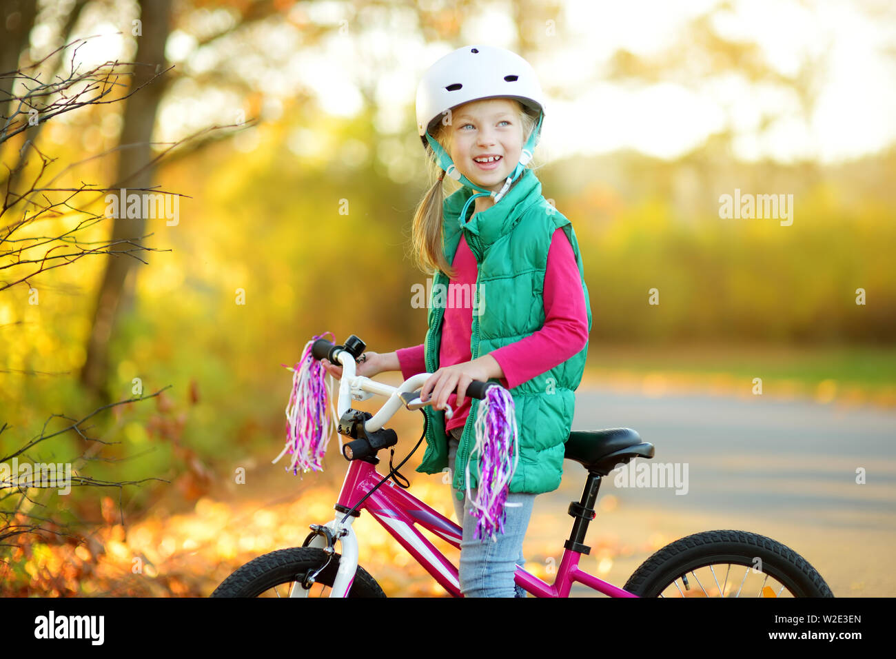 Cute little girl riding a bike in a city park on sunny autumn day ...