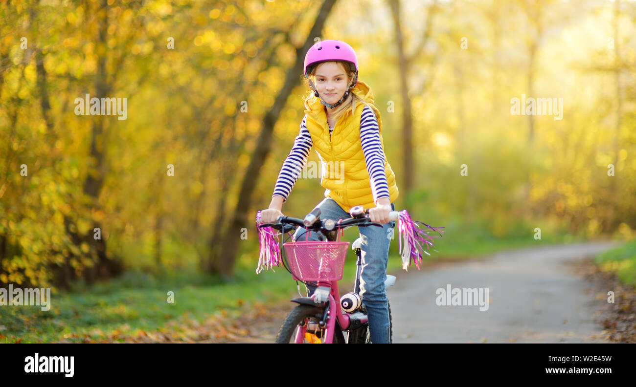 Adorable young girl riding a bike in a city park on sunny autumn day ...