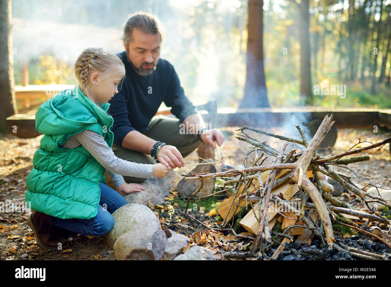 Cute young girl learning to start a bonfire. Father teaching her ...
