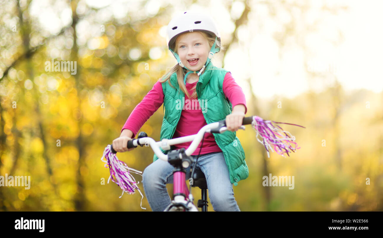 Cute little girl riding a bike in a city park on sunny autumn day ...