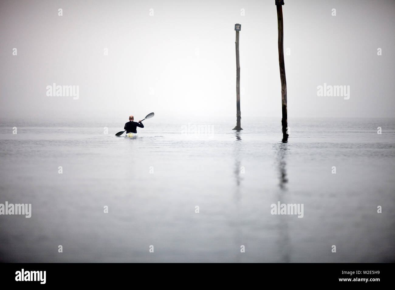 Male kayaker passes tall mooring poles as he paddles in the waters of a ...
