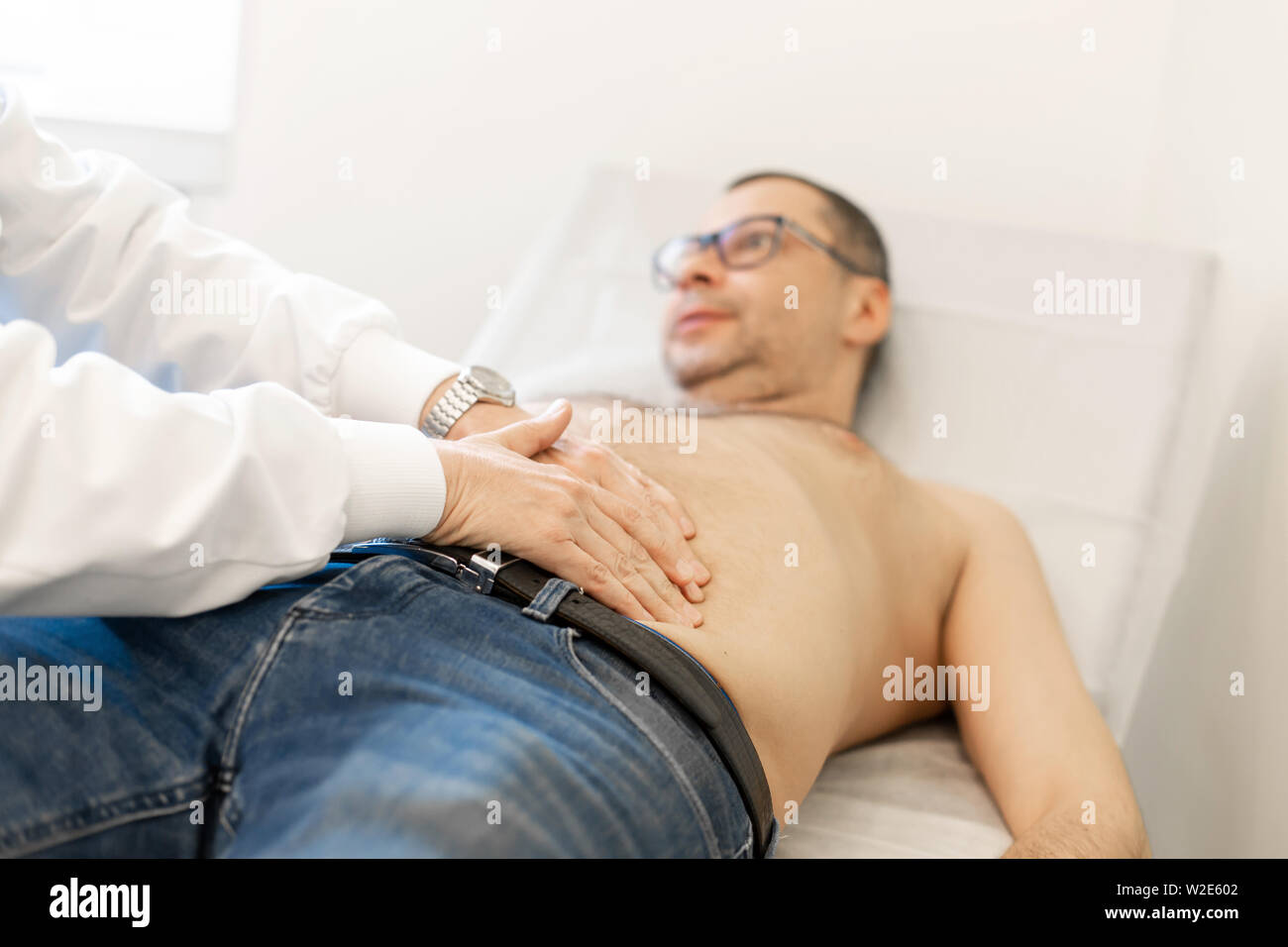 Doctor physiotherapist examining his patients stomach in medical office ...