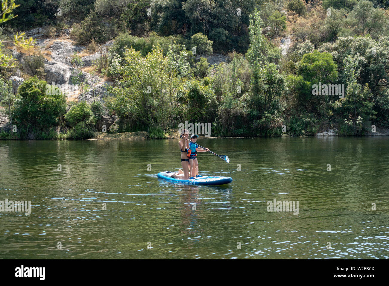 Young mother teaching a little boy how to use a Paddle Board on a lake ...