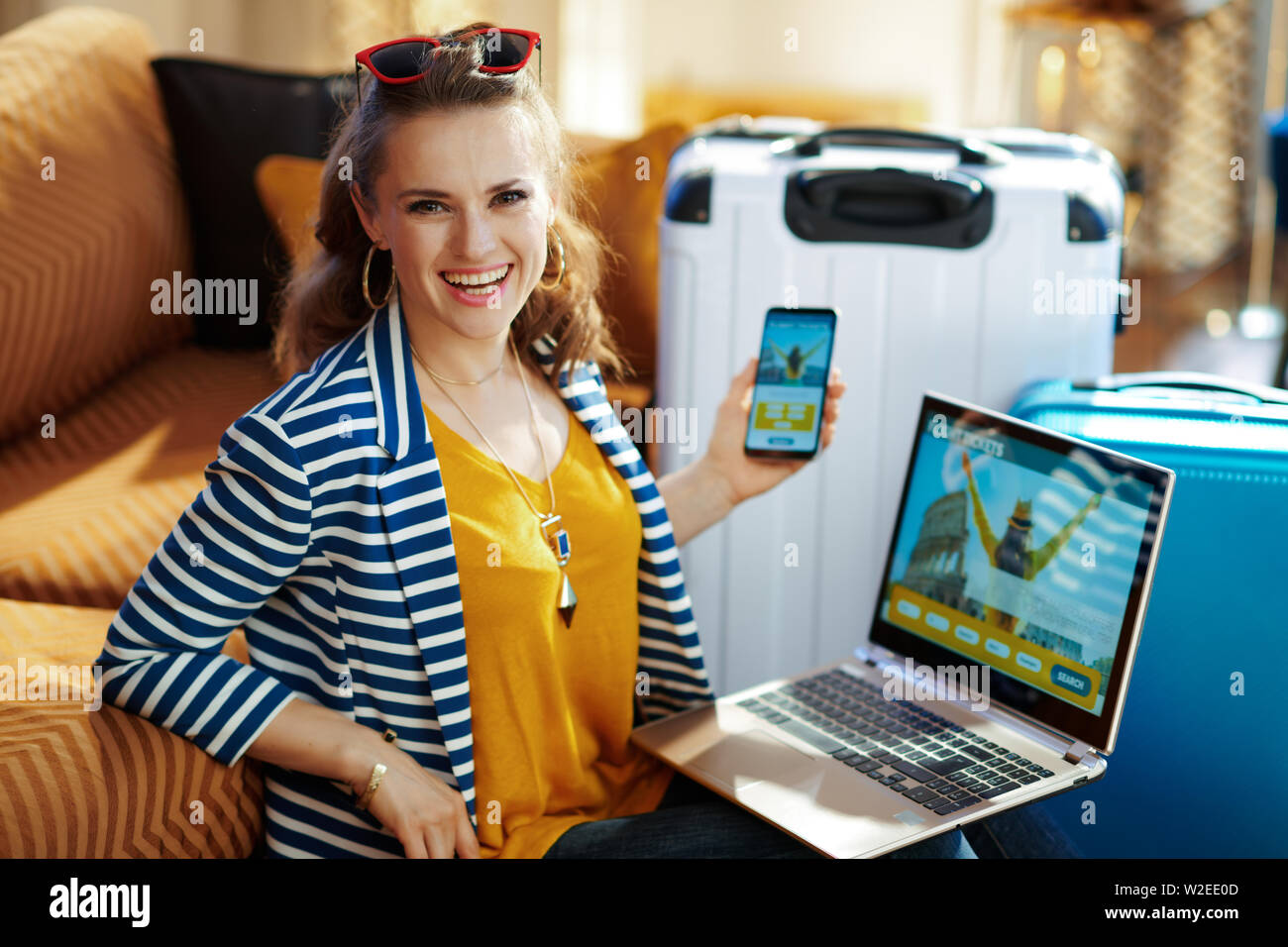 Smiling modern traveller woman in striped jacket sitting near couch and ...